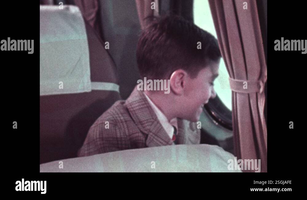 1950s: Boy looking out the window of the airplane. Pilot in the cockpit ...