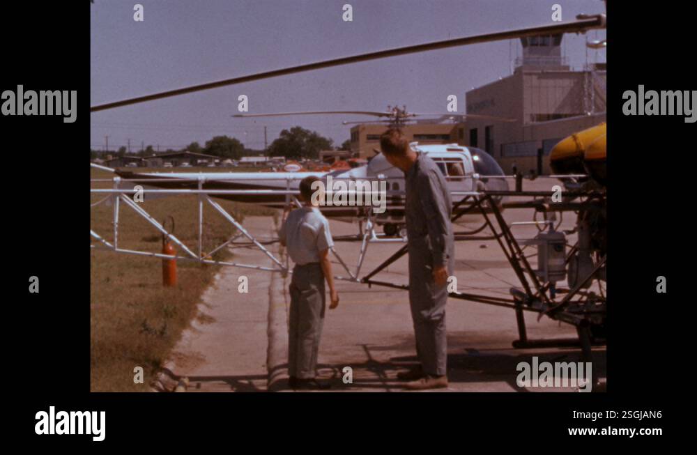 1960s: Pilot and boy standing beside helicopter. Two helicopters on the ...