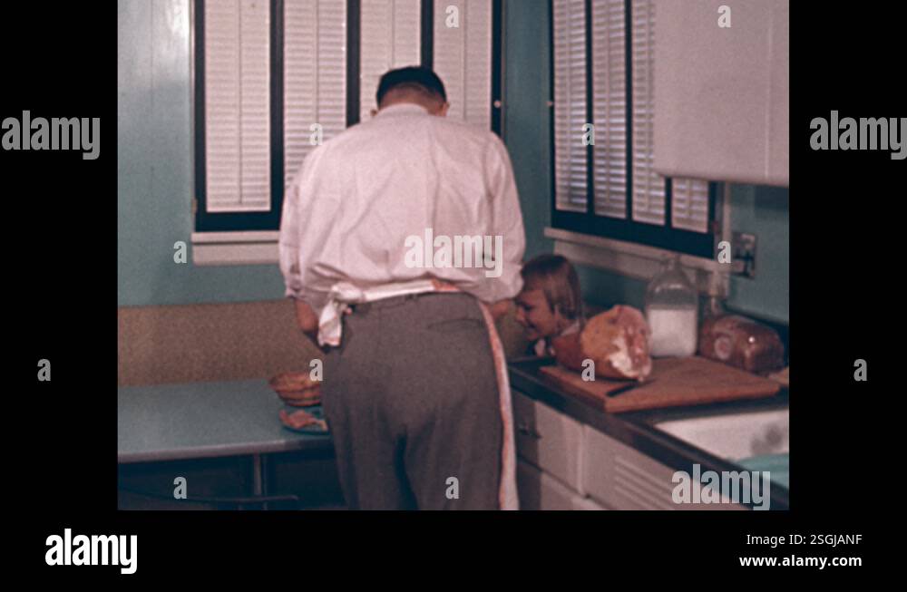 1950s: man in apron makes breakfast in 50s. Man pours milk into glass ...