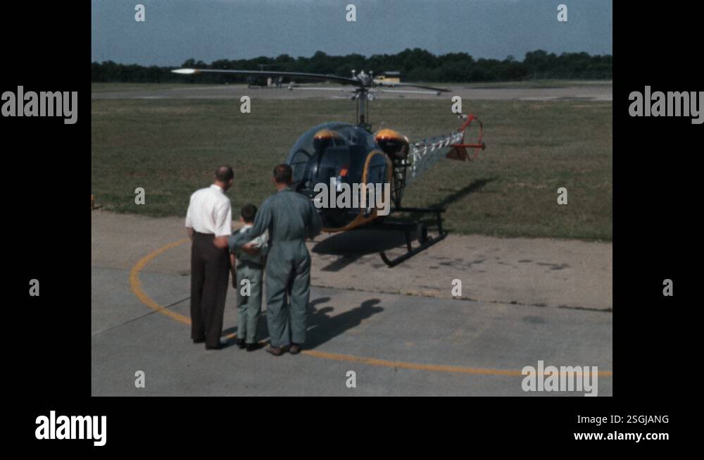 1960s: Two men and a boy walking around helicopter. Group looking into ...