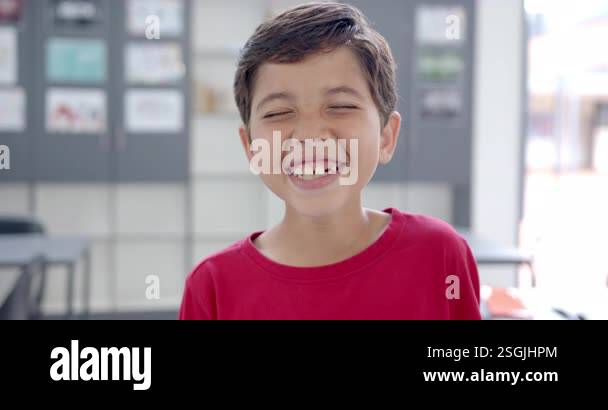 In school, young boy wearing a red shirt smiling in the classroom. Behind him, math signs ...