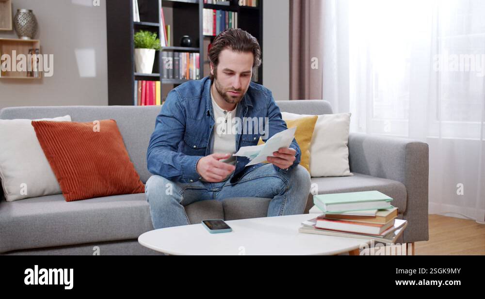 Beautiful focused man calculating bills and taxes on phone. Attentive ...