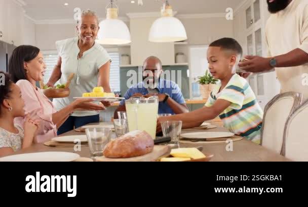 A diverse family gathered around dining table, smiling and interacting ...