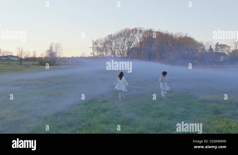 Two Happy women running in a field with fog running away from camera ...