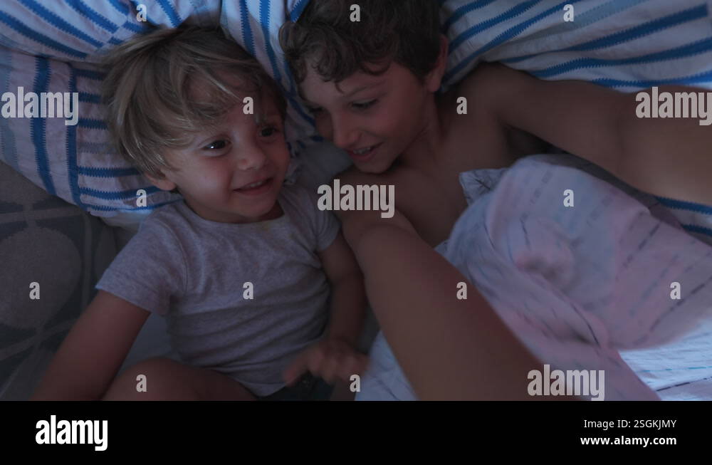 Two happy young brothers under bed blankets. Candid family moment ...