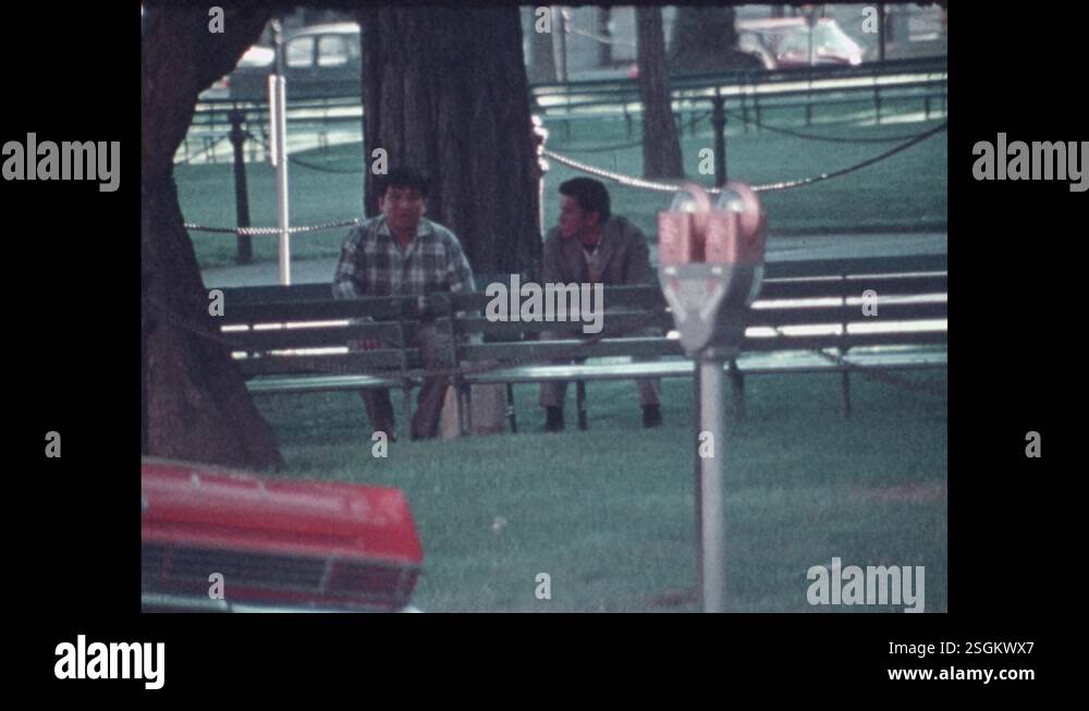 1970s: Men sitting on bench in park. Kids playing with fire hydrant in ...