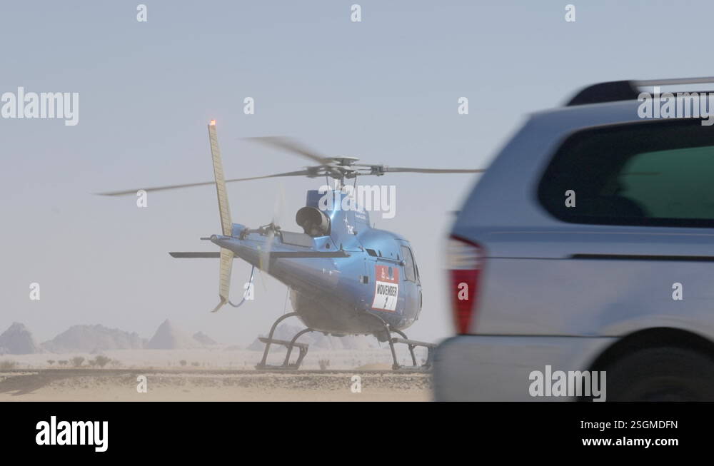 A helicopter about to take off with dusty desert landscape and car ...