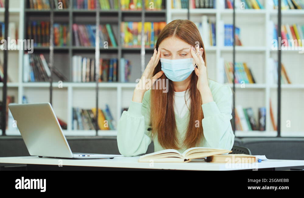 Young female student in mask working on laptop having headache Stock ...