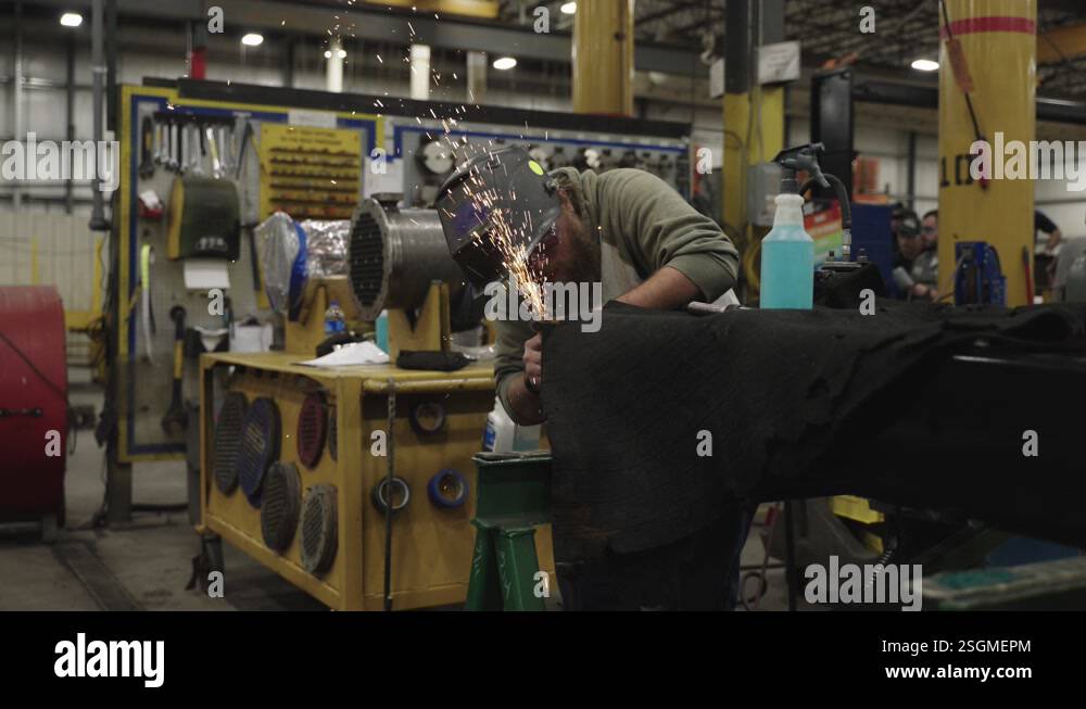 Blue collar worker welding metal in workshop, sparks flying in slow ...