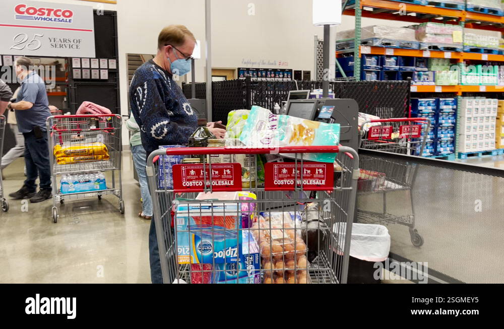 Man with mask at self-checkout line at Costco. Shopping cart full of ...