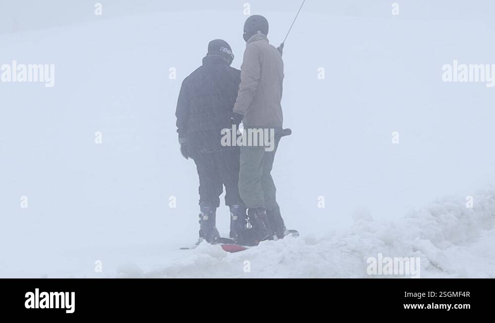 Skier and Snowboarder on a T-Bar lift in a snowy mountain ski resort ...