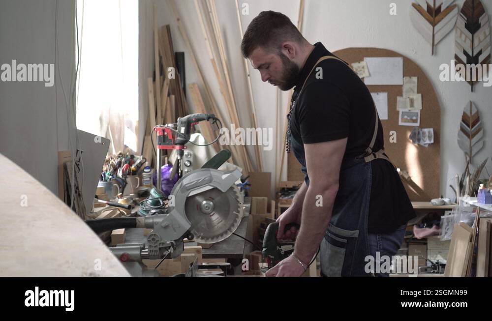 A man in a carpentry workshop saws a board with a jigsaw. The carpenter ...
