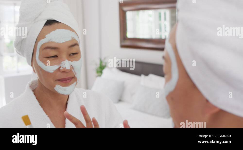 Video of happy asian woman in robe with moisturizing mask looking at mirror Stock Video Footage ...