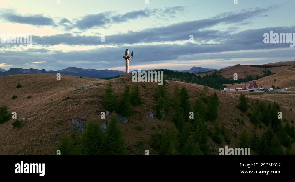 Aerial orbit shot of waving Romanian flag and cross on top of Dichiu ...