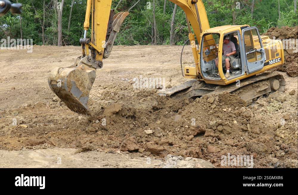 John Deere hydraulic excavator digging dirt from bottom of pond and ...