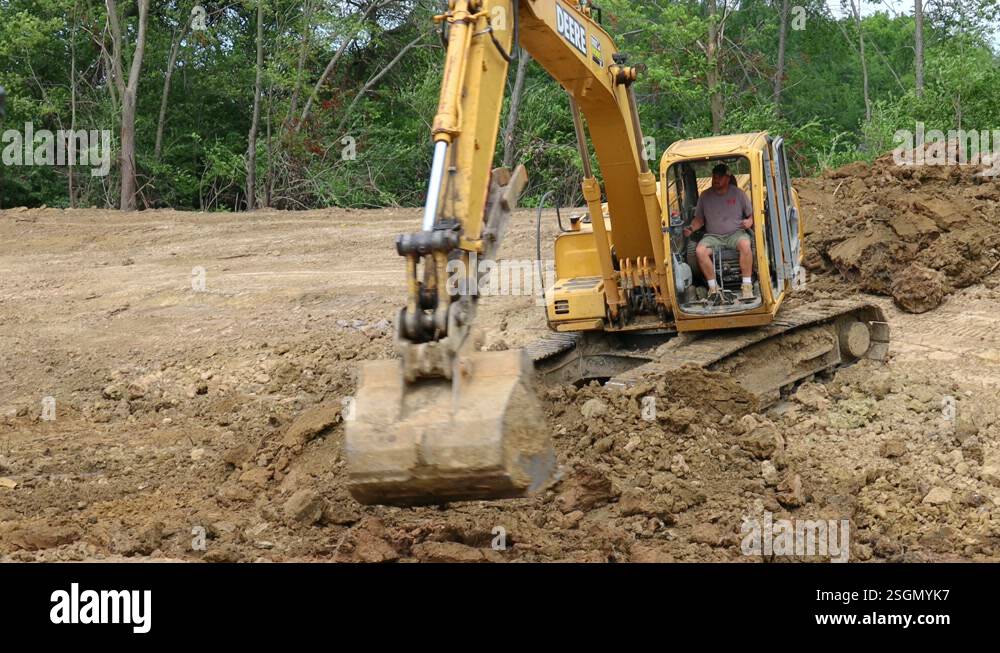 John Deere hydraulic excavator digging dirt from bottom of pond and ...