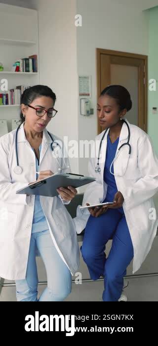 Vertical view two multiethnic women GP doctors in uniform talking ...