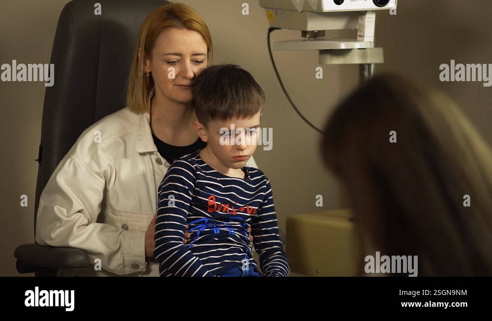 Female eye doctor checks boy's vision while he sits on mother's lap ...