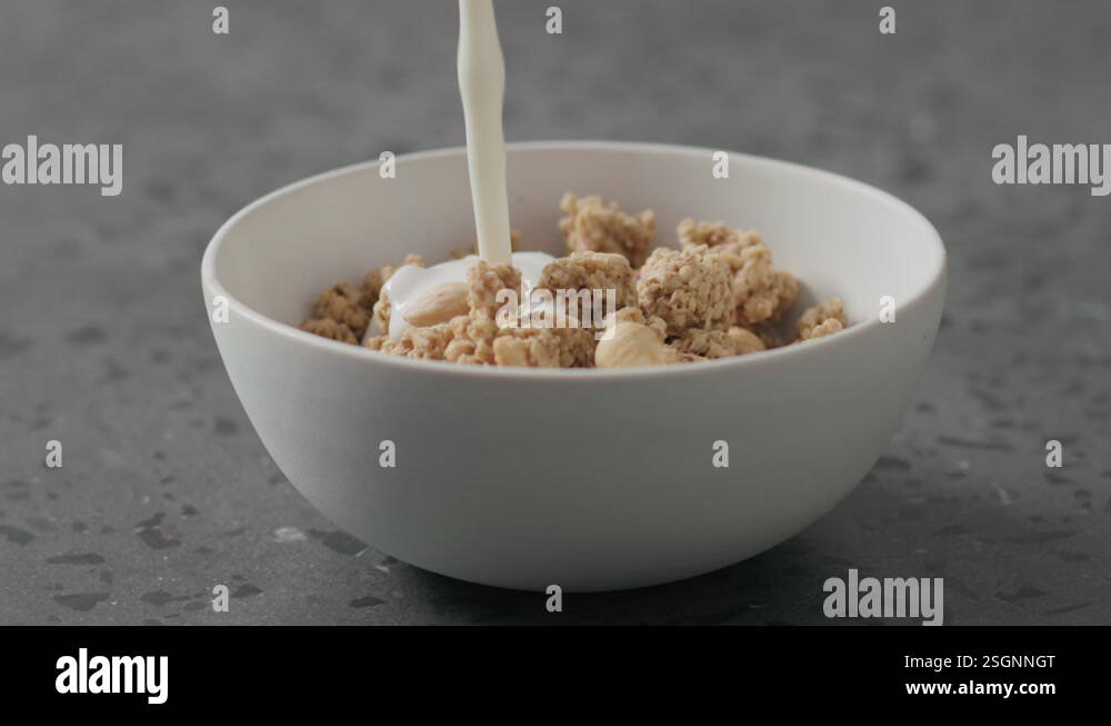 Slow motion pour yogurt in white bowl with nutty granola on terrazzo ...