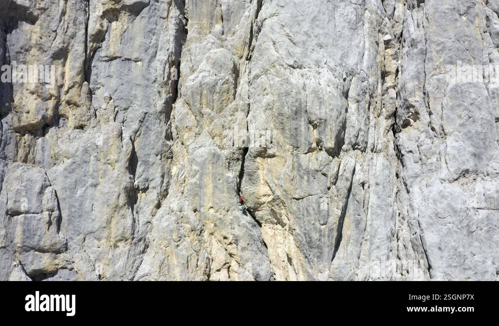 Aerial backwards shot of mountaineer climbing on steep cliff wall ...