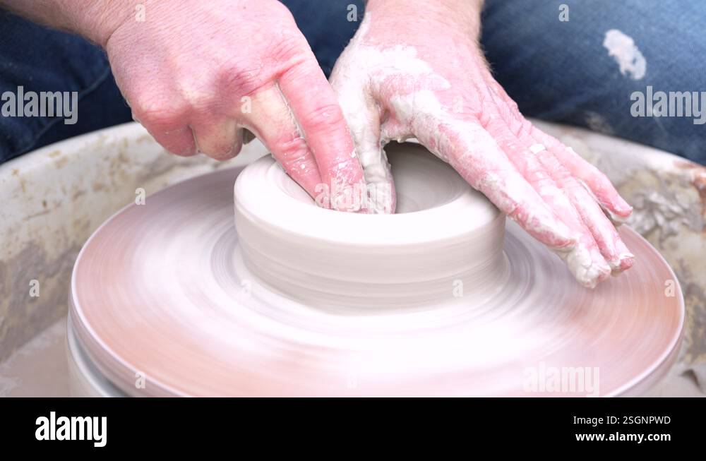 Close of a potter's hands making handmade pots on his pottery wheel ...