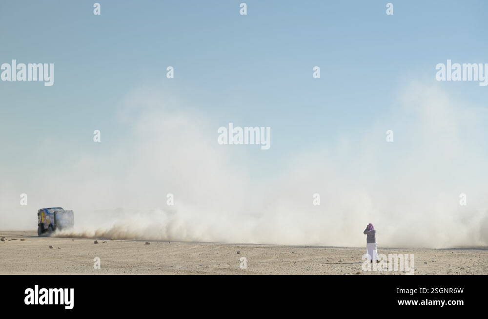 A blue Dakar Rally truck racing past an Arabic man taking photos with ...