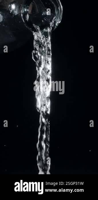 Pure water is being poured out from a glass bottle on black background ...