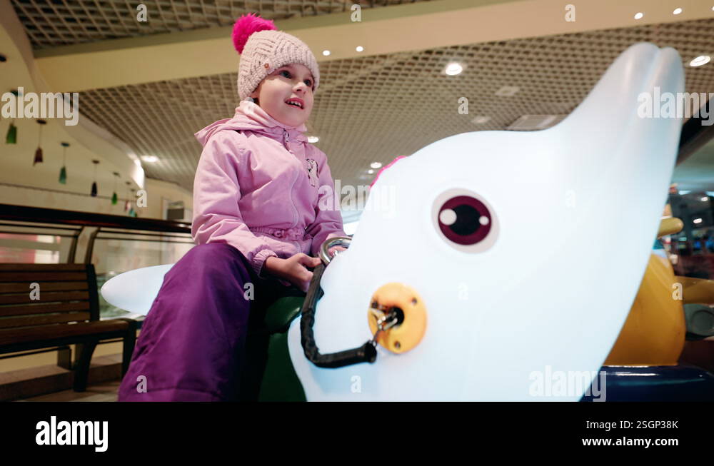 Focused cute girl is having fun on a dolphin carousel in mall Stock ...