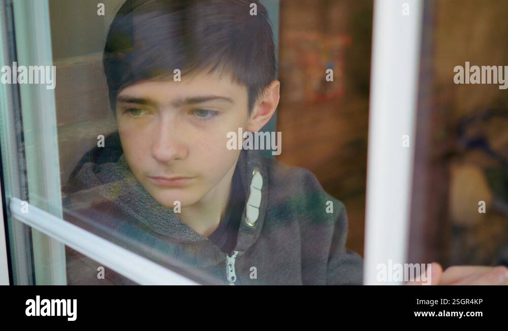 Sad boy looking through window from room. Unhappy face of schoolboy ...