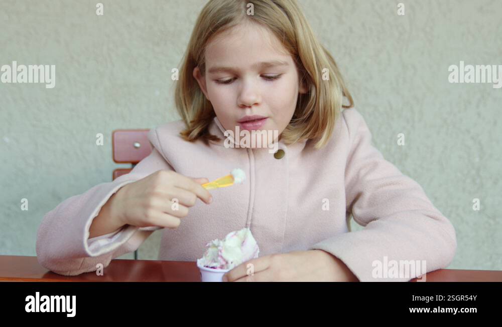 a child girl eats ice cream from a paper cup with a plastic spoon Stock ...
