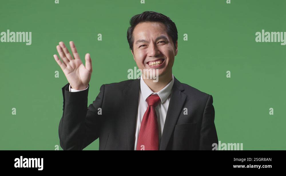 An Asian Business Man Waving Hand And Smiling While Standing On Green ...