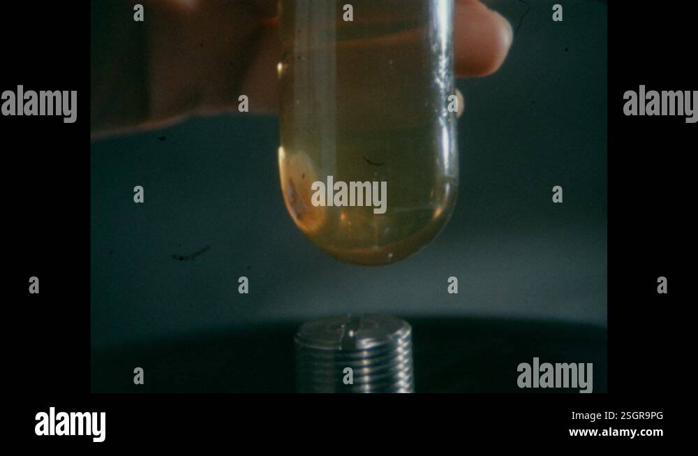 1950s: Hand pulls vial of liquid from machine. Sediments at the bottom ...