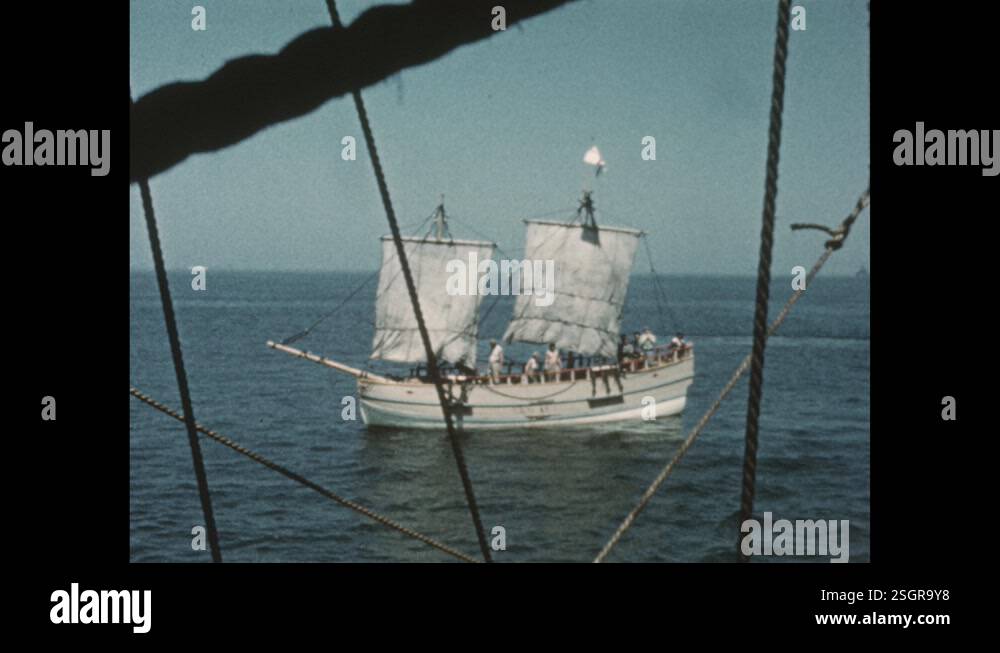 1970s: Boats on the water. Man stands atop mast of ship. Man on deck of ...
