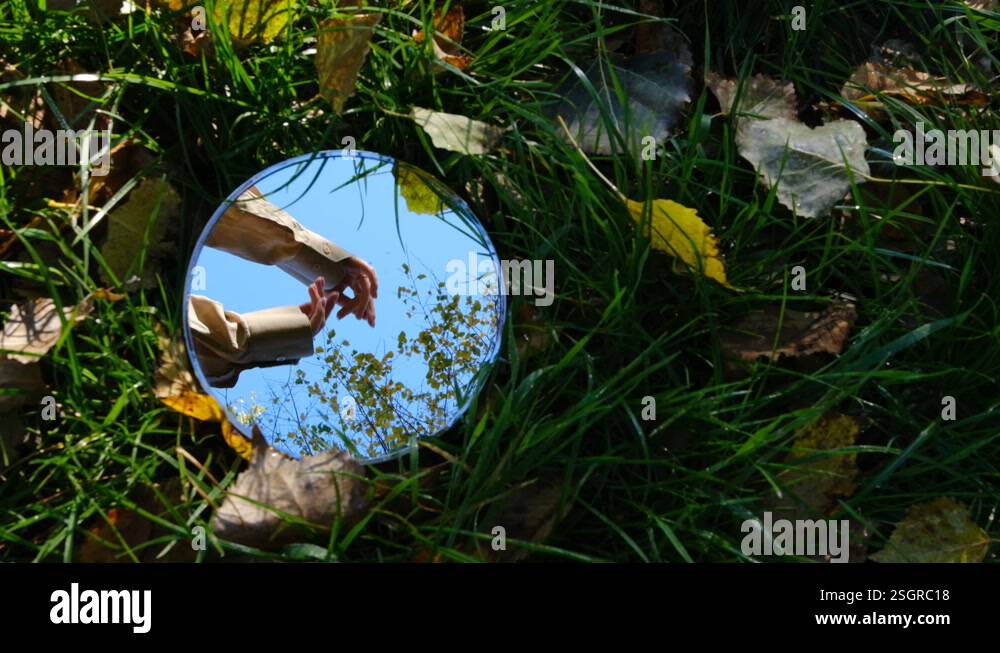 The reflections of woman hands moving in round mirror lying in nature ...