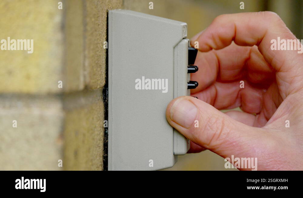 Hands keying in the code to open an outside wall safe then remove a key ...