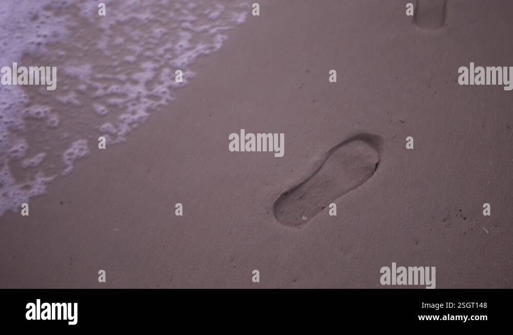 Slow-motion tracking shot of foot prints on the beach with waves ...