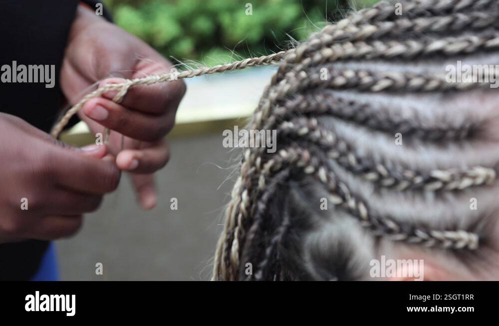 African master quickly and neatly weaves a long Afro braid on the girl ...