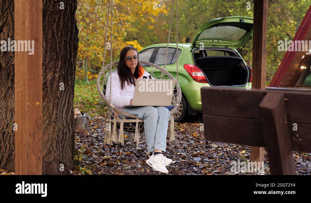 A woman in the courtyard of a country house is sitting with a laptop on ...
