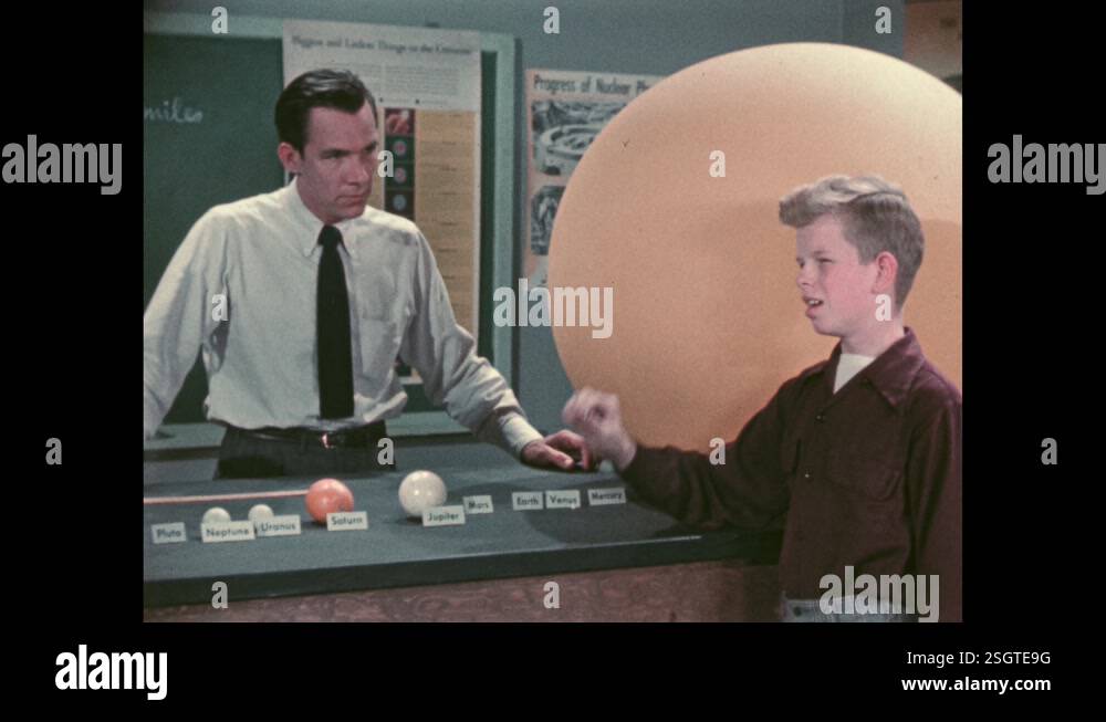 1950s: Classroom, teacher stands over lab table. Solar system model ...
