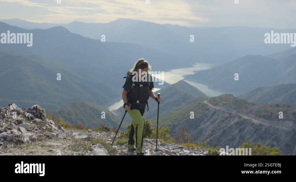 Active girl with hiking poles and backpack walking uphill with a view ...