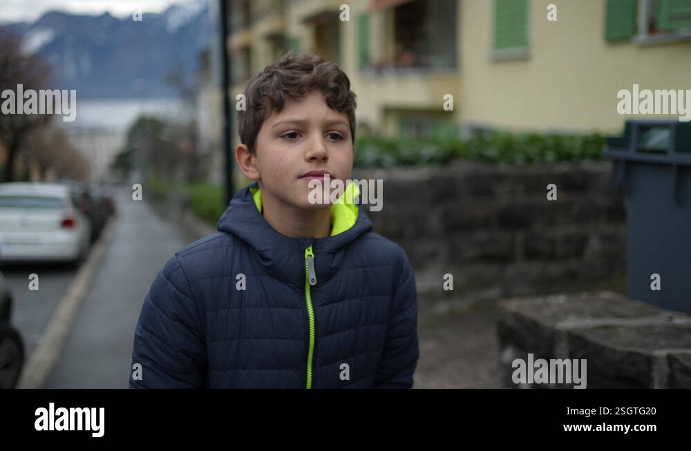 One pensive young boy walking in city street forward. Preteen male kid ...