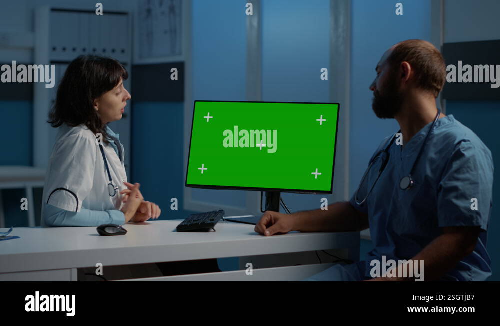 Medic and assistant looking at computer monitor with green screen ...