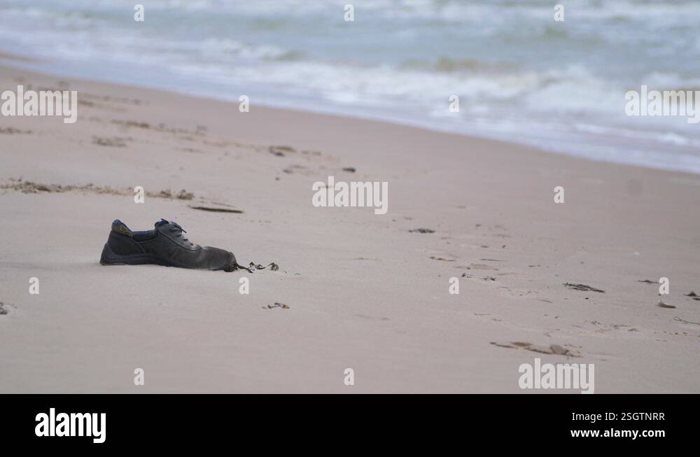 Black shoe on the beach, trash and waste litter on an empty Baltic sea ...