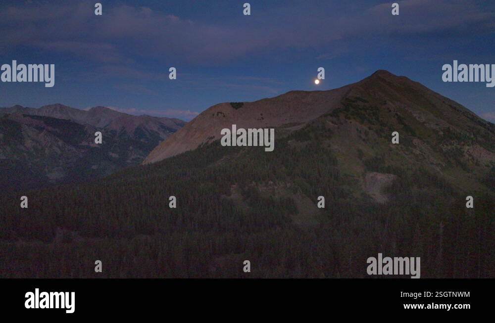 A full moon sits just above a mountain peak in the Colorado Rockies on ...