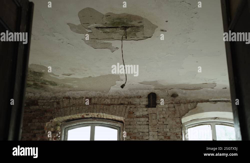 Wire with empty light bulb socket hangs from old ceiling with crumbling ...