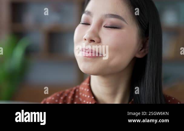 Young adult smiling asian woman relaxing with her eyes closed in living ...