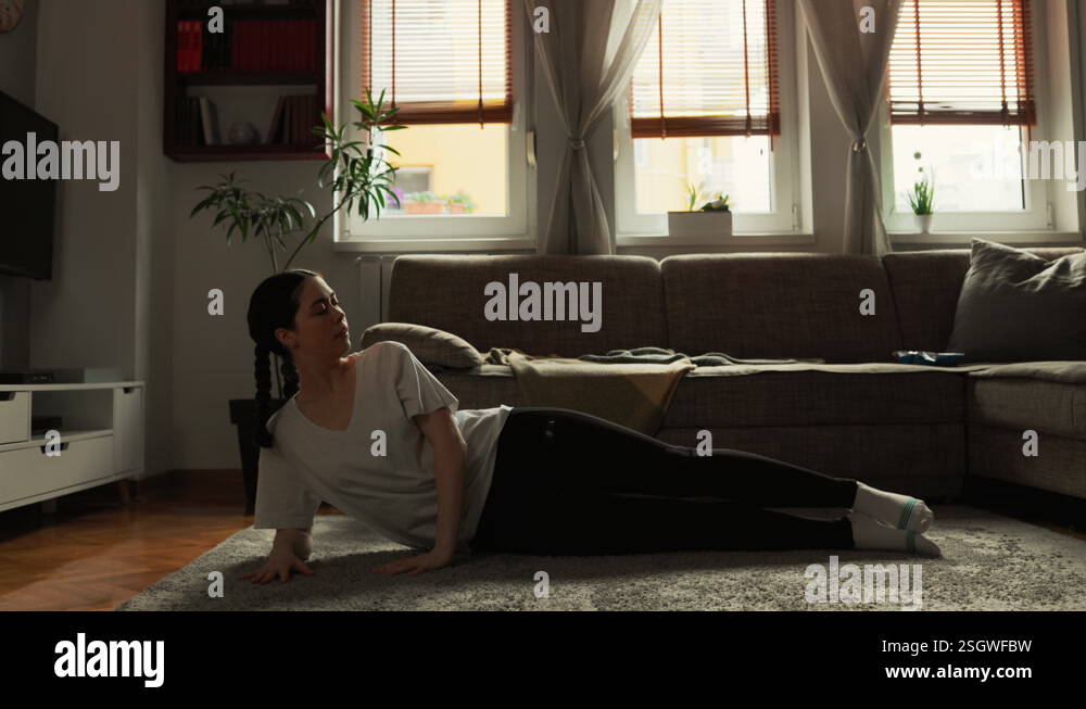 Young Caucasian woman does scissors-exercise lifting legs lying on ...