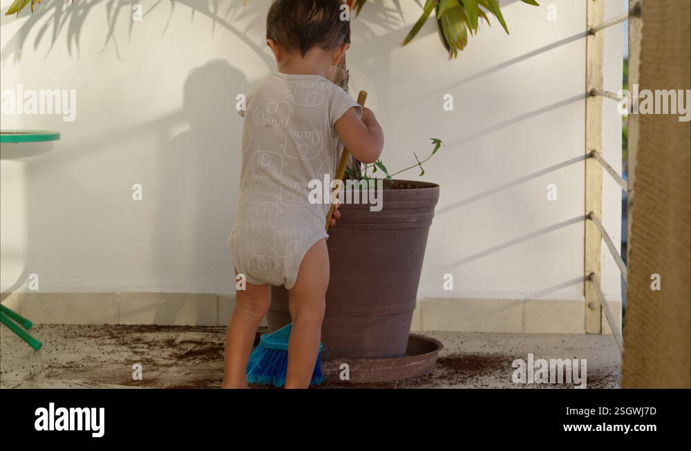 Little young latin toddler in a baby romper sweeping with a toy broom ...