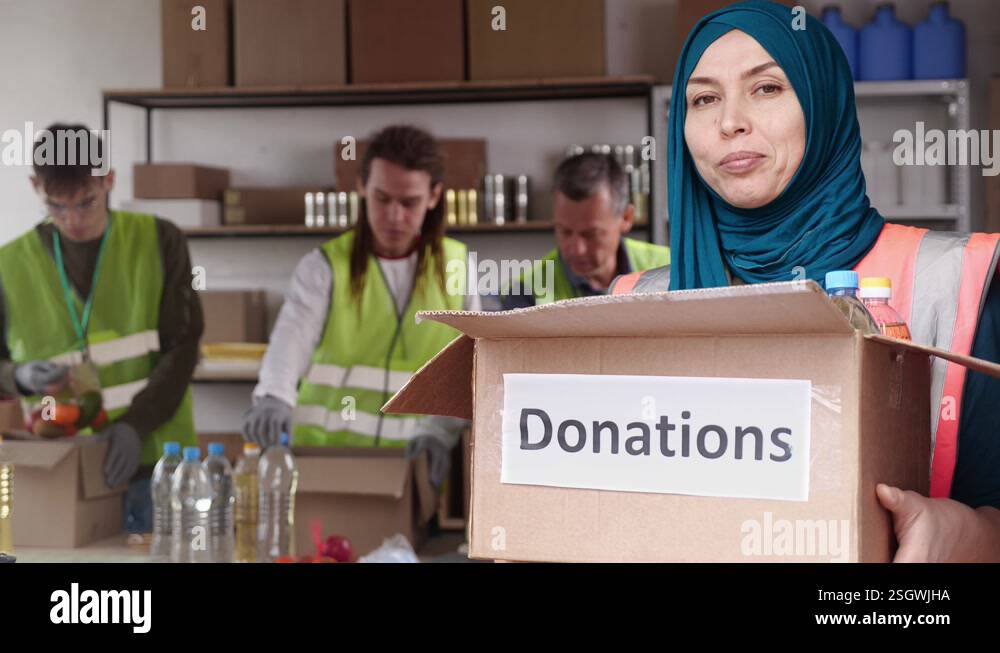 A Muslim woman volunteer in a hijab holds a donation box and smiles ...