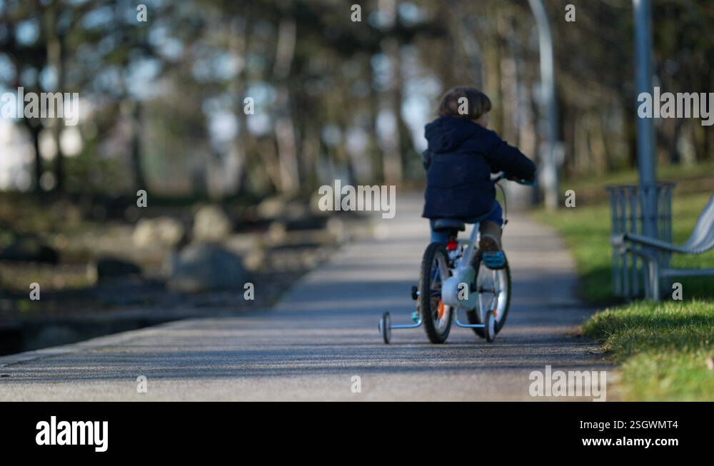 Back of child riding bicycle outside at city park. One little boy rides ...